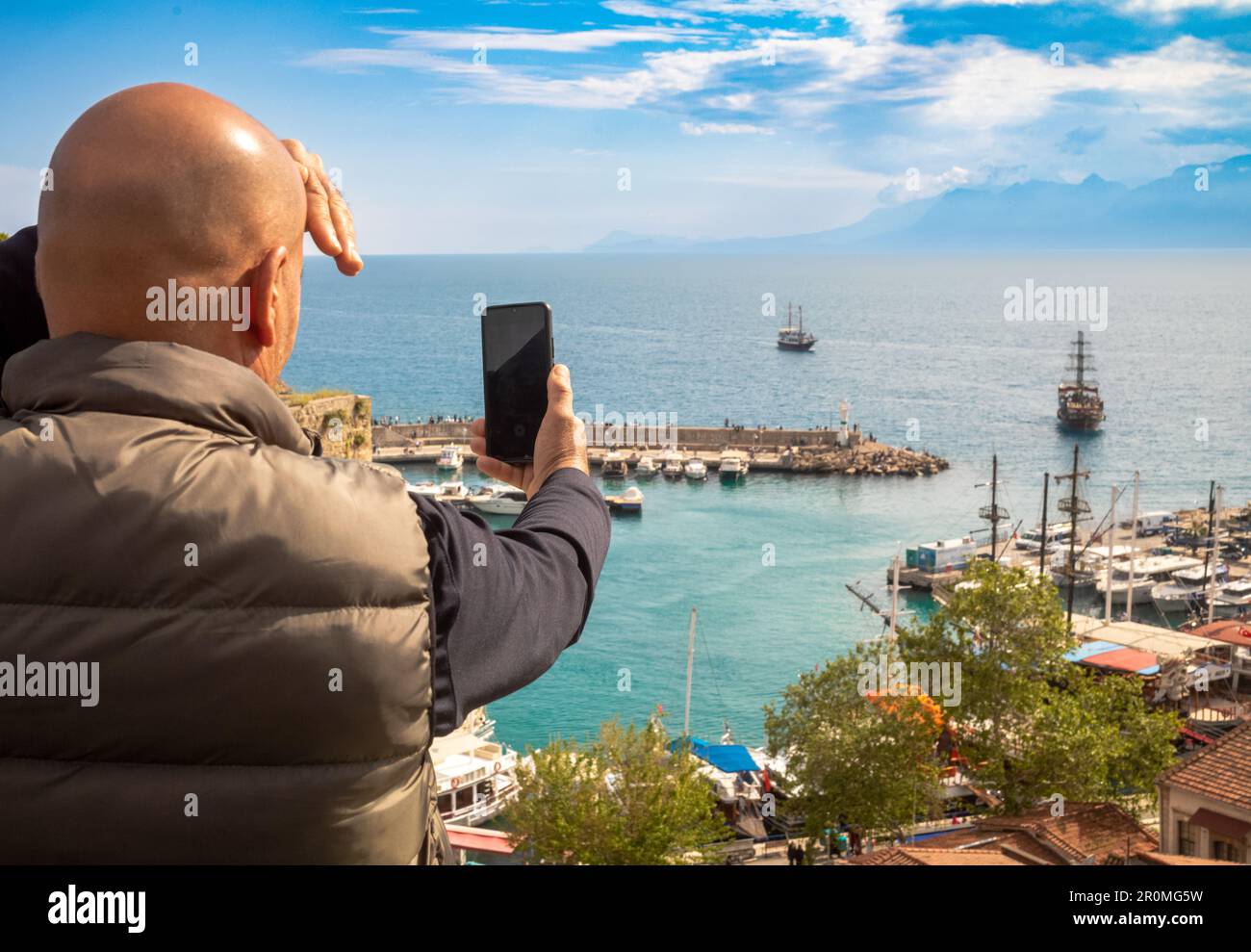 A man with a bald head takes a photograph of tourist boats returning to ...