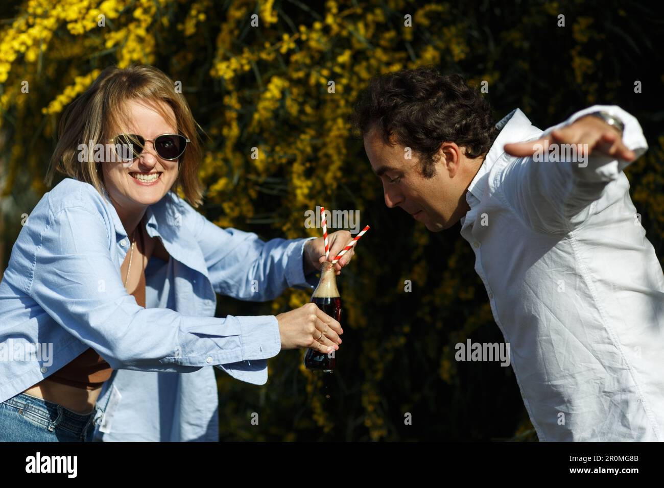 Young happy couple outdoors drinking cold drink from glass bottle with ...