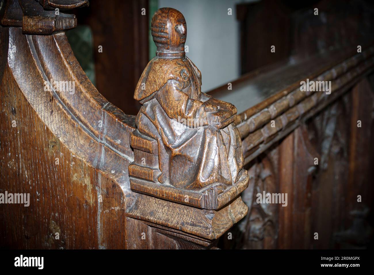 Carved wooden bench end of a seated cleric with open book on his lap at ...