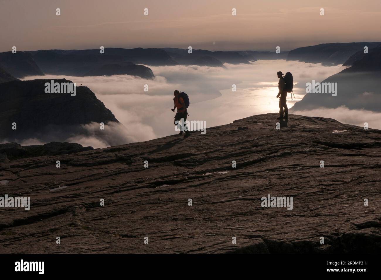 2 hikers with backpack go in the backlight of the sunrise along the ...
