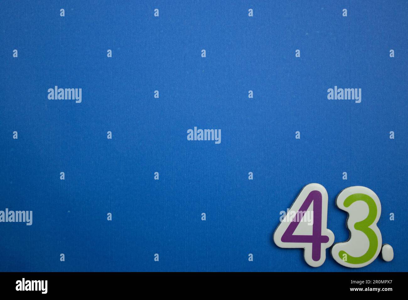 The number 43, placed on the edge of a blue background, photographed from above, colored purple ...