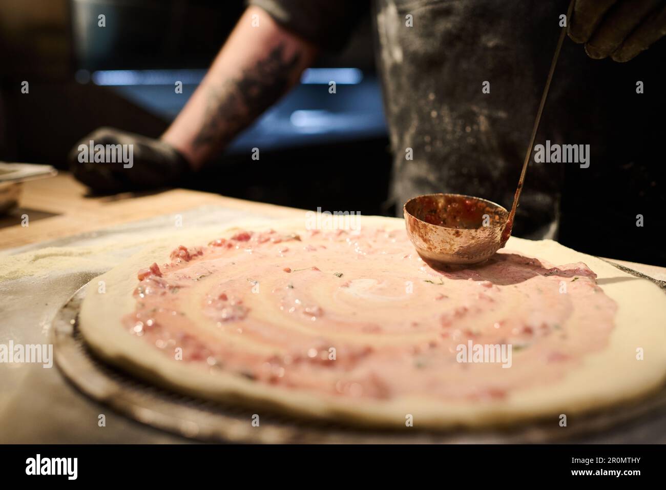 Chef of restaurant spreading mixture of ingredients on flatbread with ...
