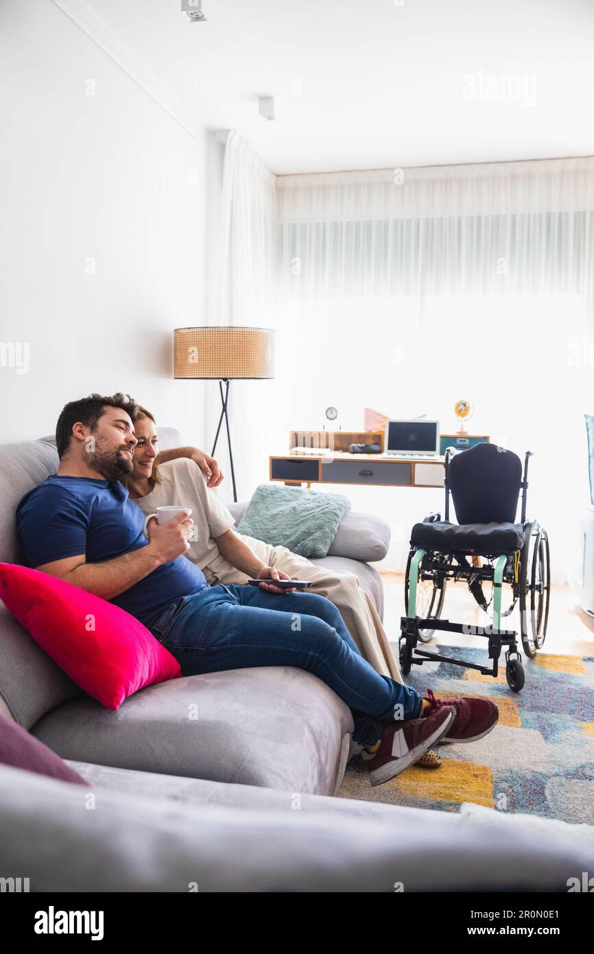 Loving Couple Cuddling And Relaxing Together On Comfortable Sofa In Living Room While Watching