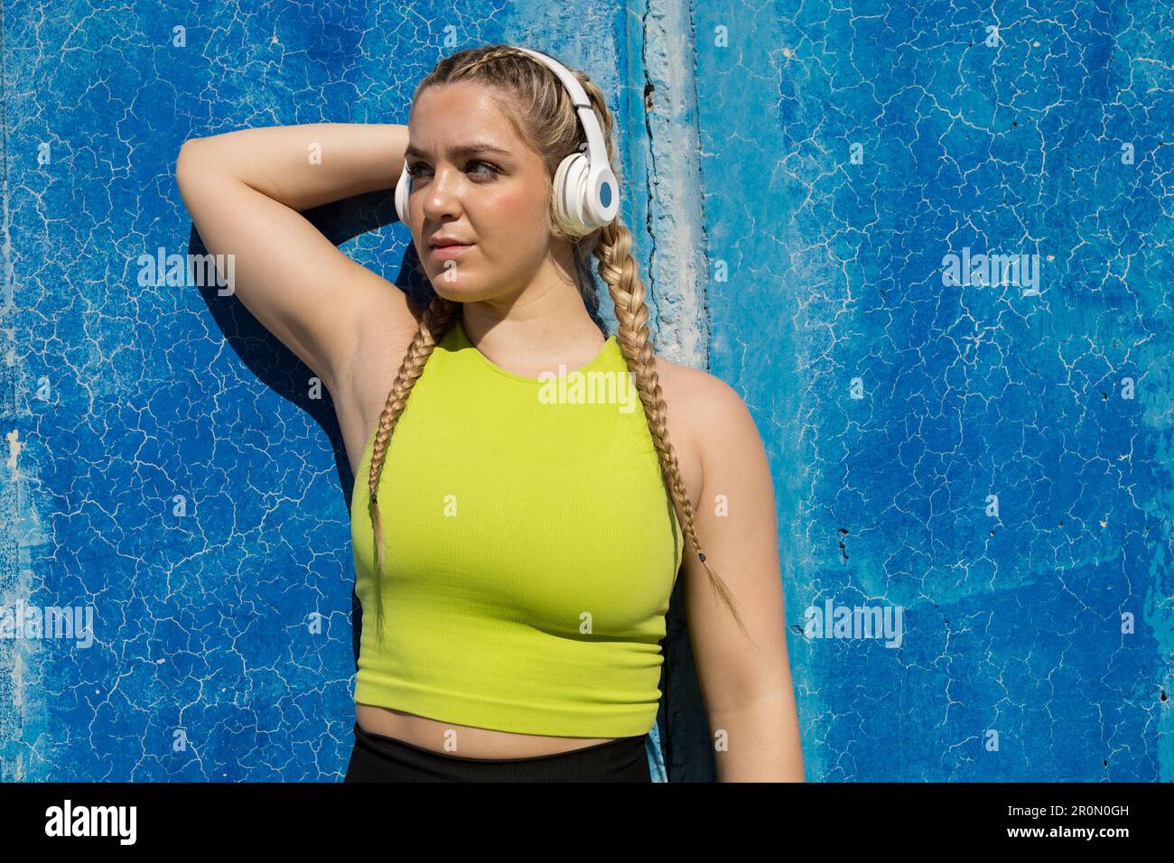 Confident young female in sportswear listening to music over headphones ...