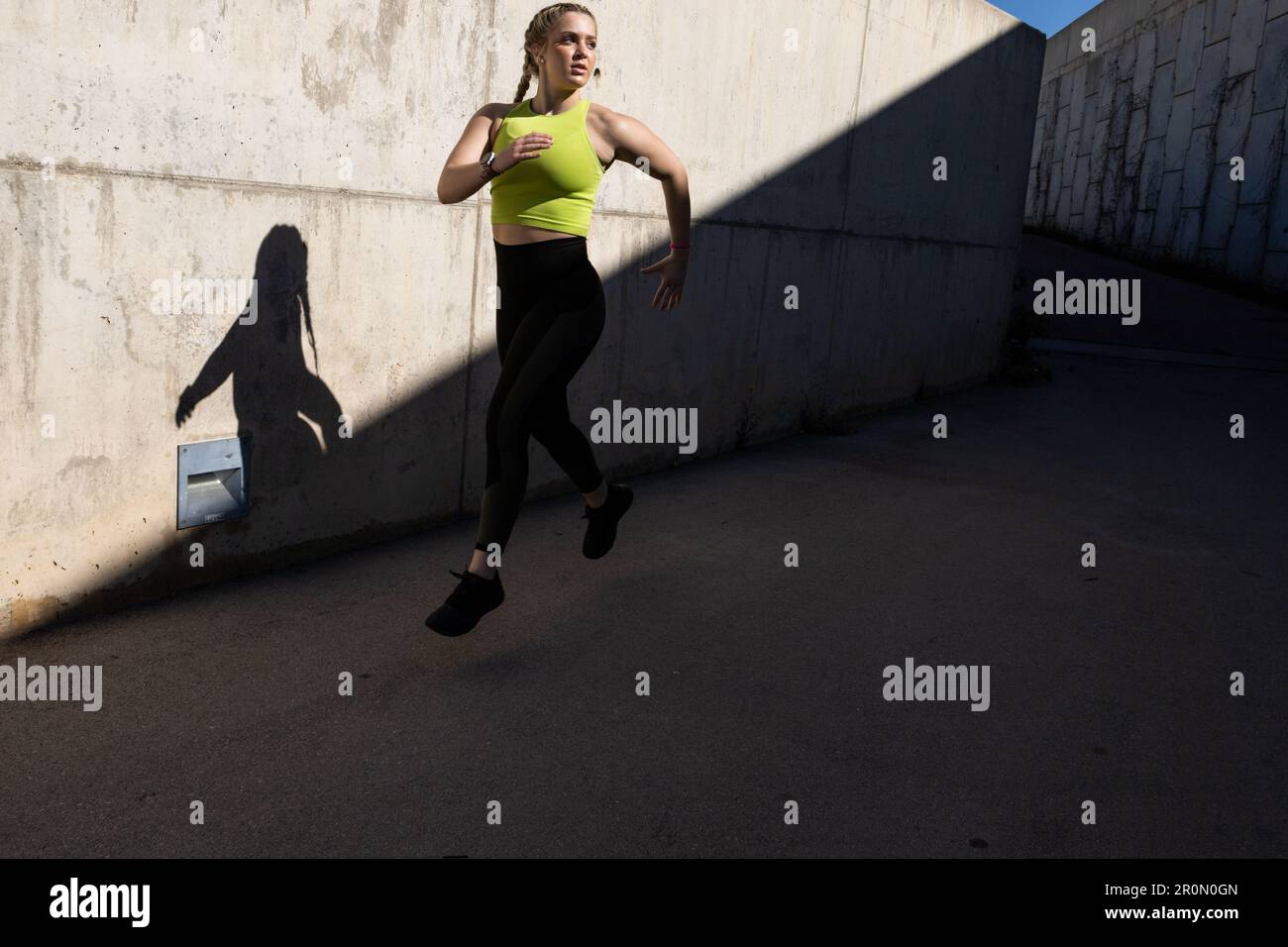 Full body of young fit female athlete in sportswear jogging on asphalt ...