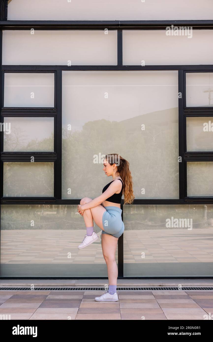 Full body side view of young woman in sportswear standing on one leg ...