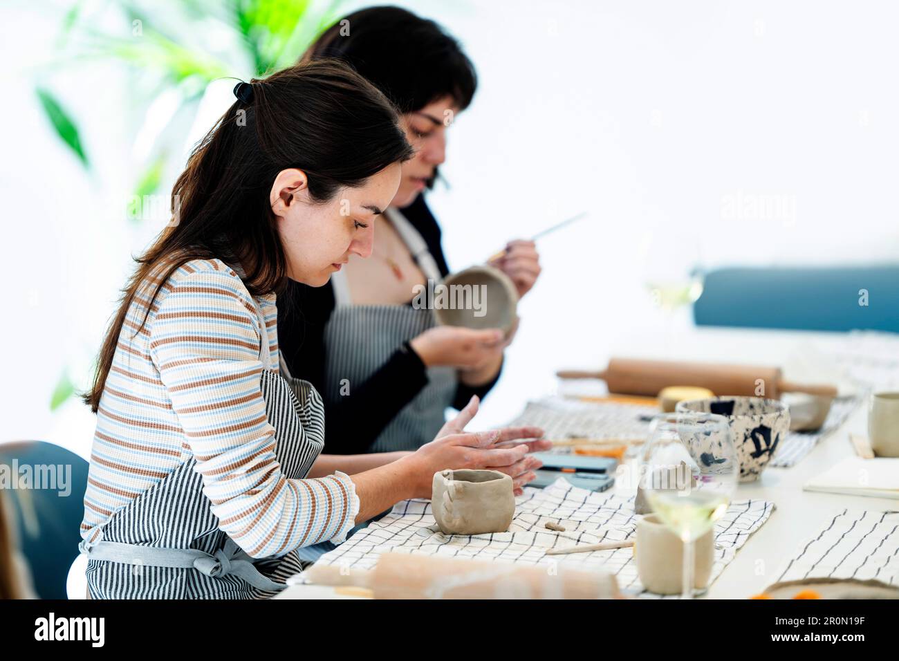 Concentrated female artists in aprons creating handmade clay cups while ...