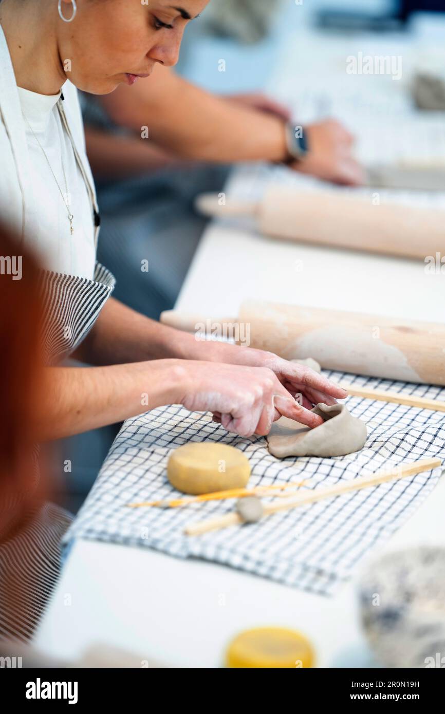 Crop concentrated female artisan making hole in piece of clay while ...