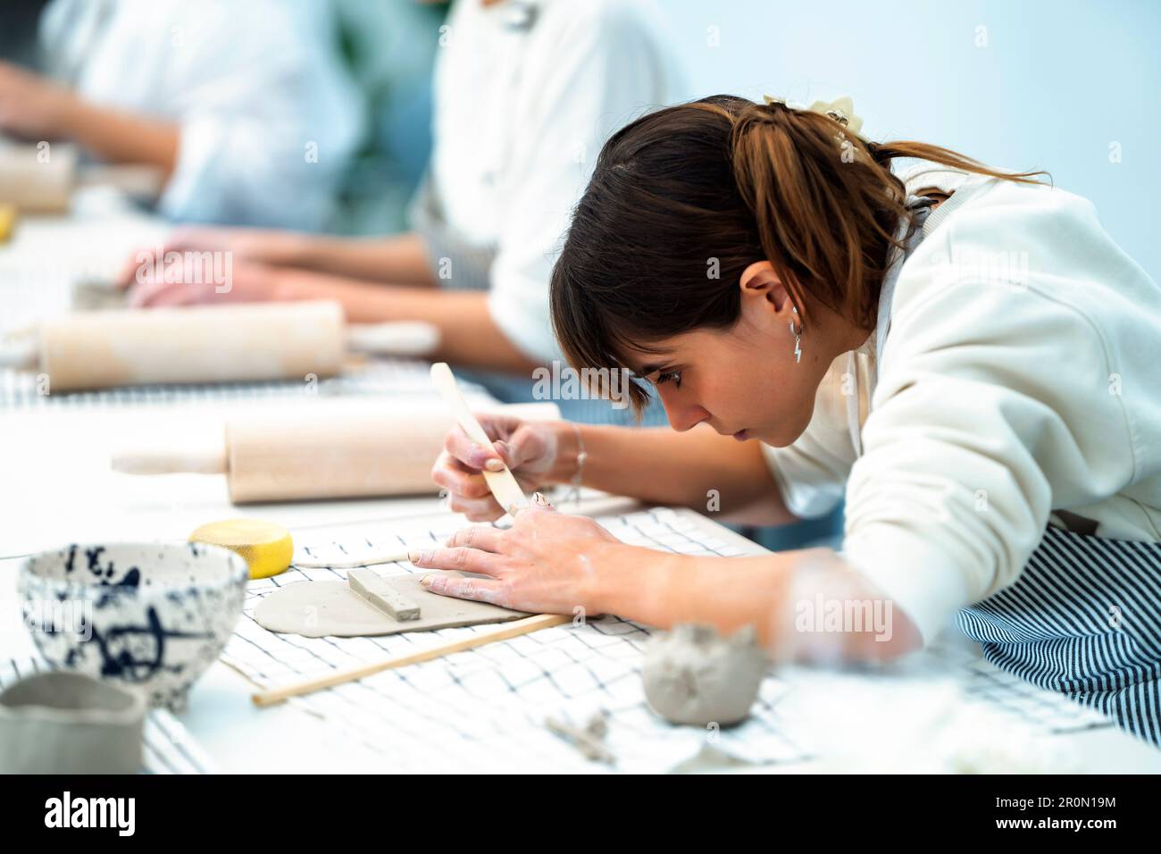 Focused young female artisan in apron creating handmade clay pot while ...