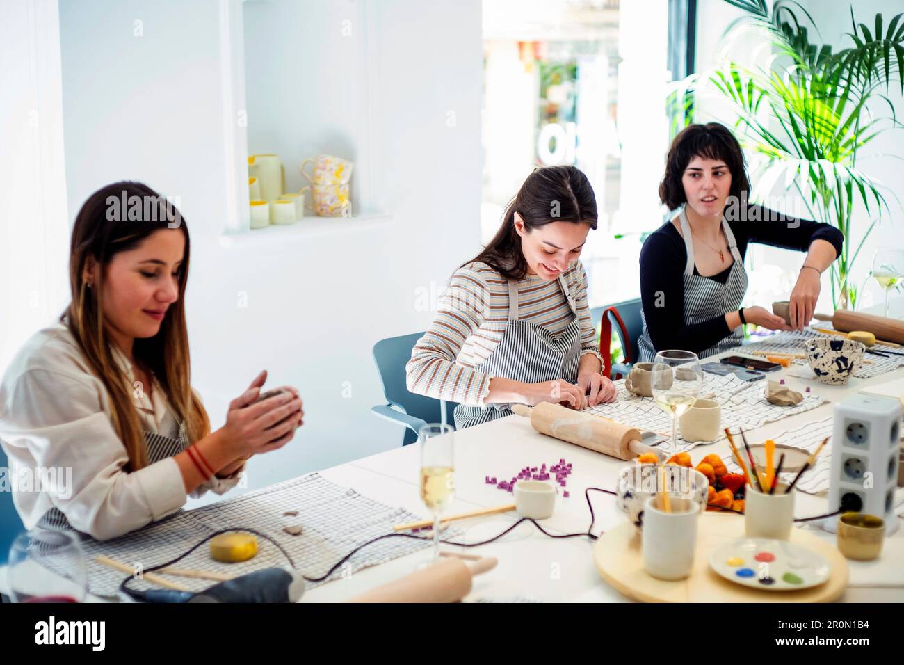 Group of positive young female artists in aprons gathering at table ...