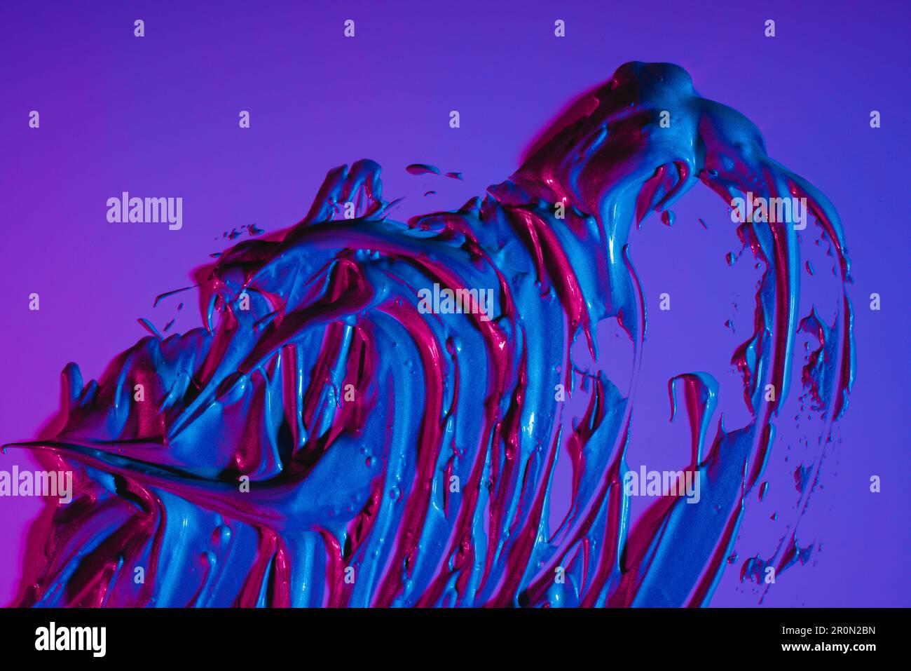 From above puddle of bright neon acrylic paint spread on vivid purple ...