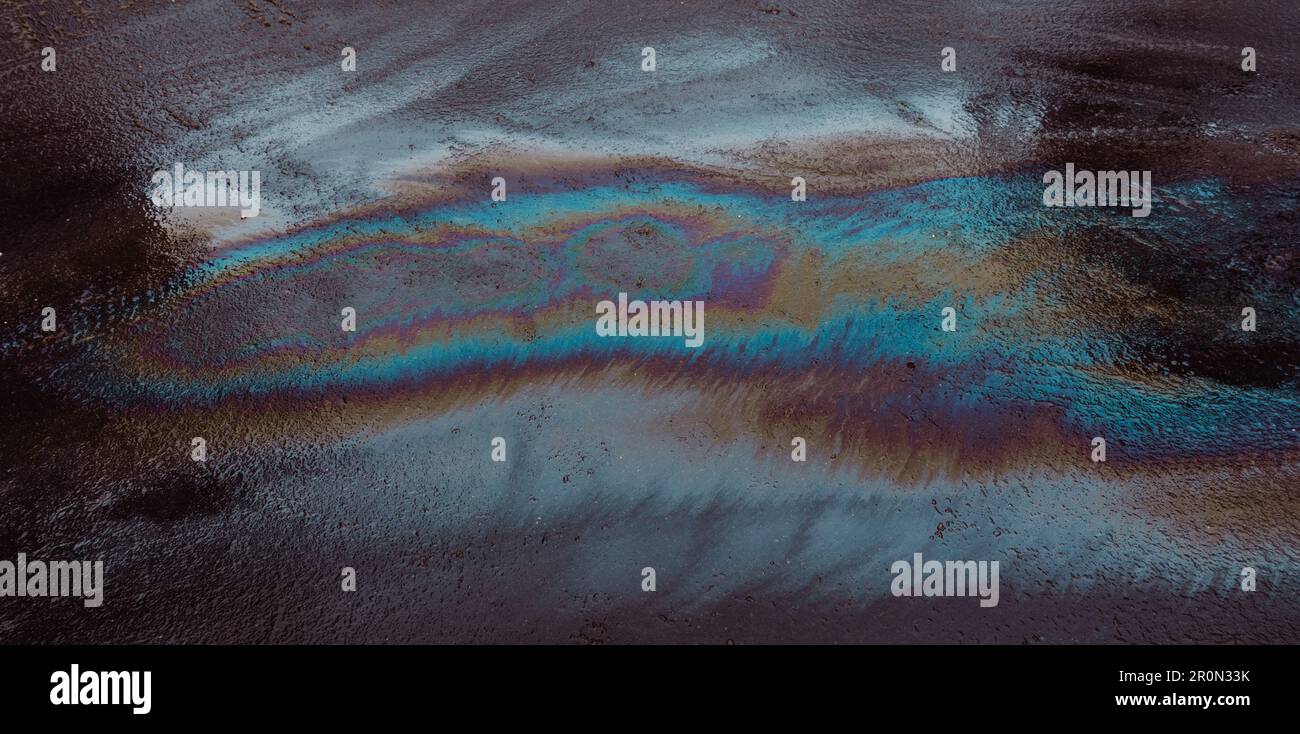 Colorful oil spill spreading on surface of wet asphalt on city street ...