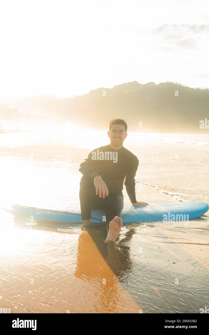 Full body of young male surfer in wetsuit looking at camera while ...