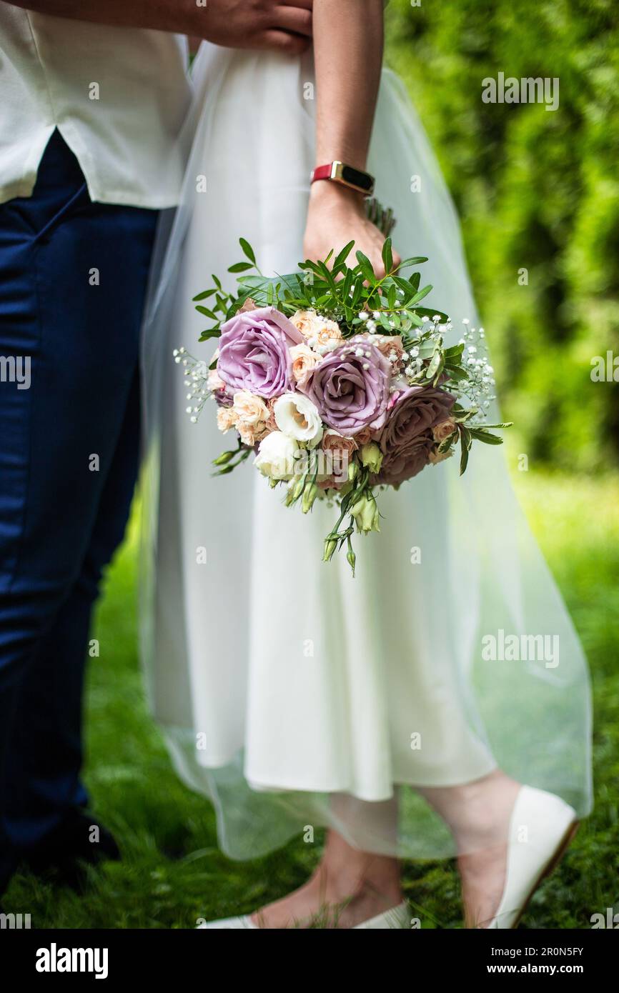 Marriage couple legs standing together on green lawn, bride holding ...