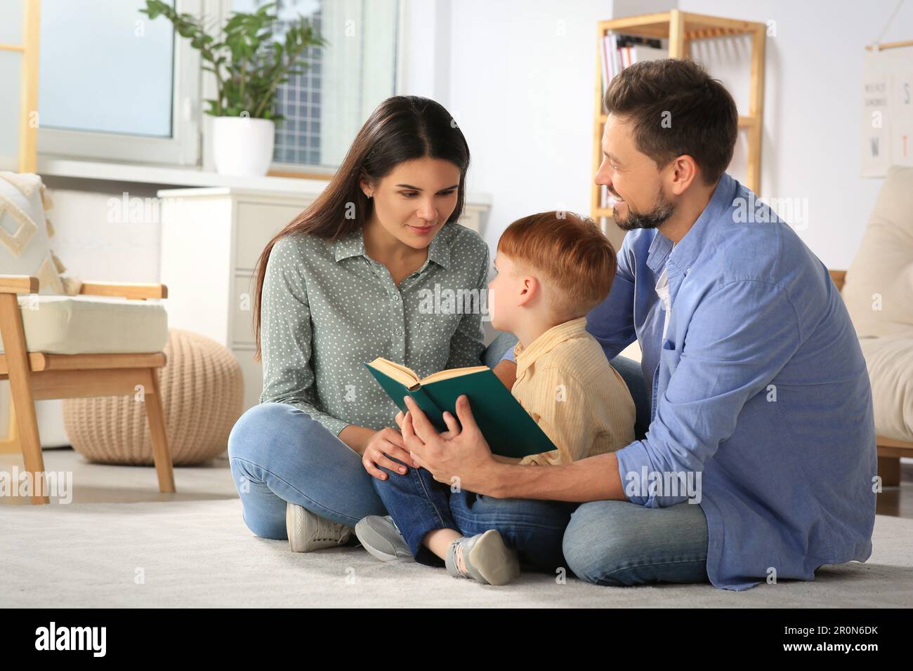 Happy family reading book together on floor in living room at home ...