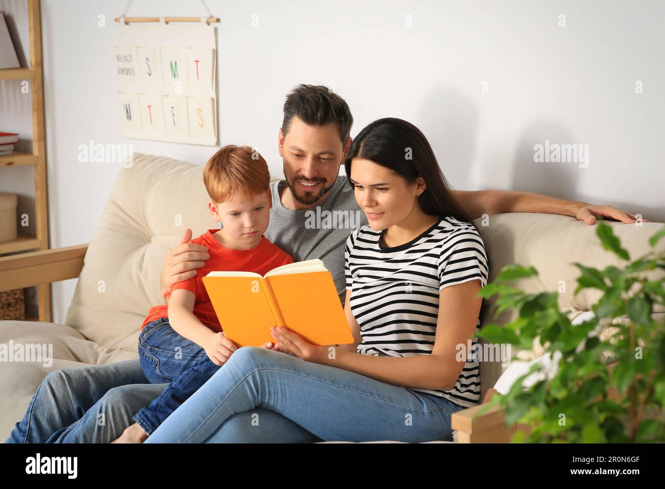 Happy family reading book together on sofa in living room at home Stock ...