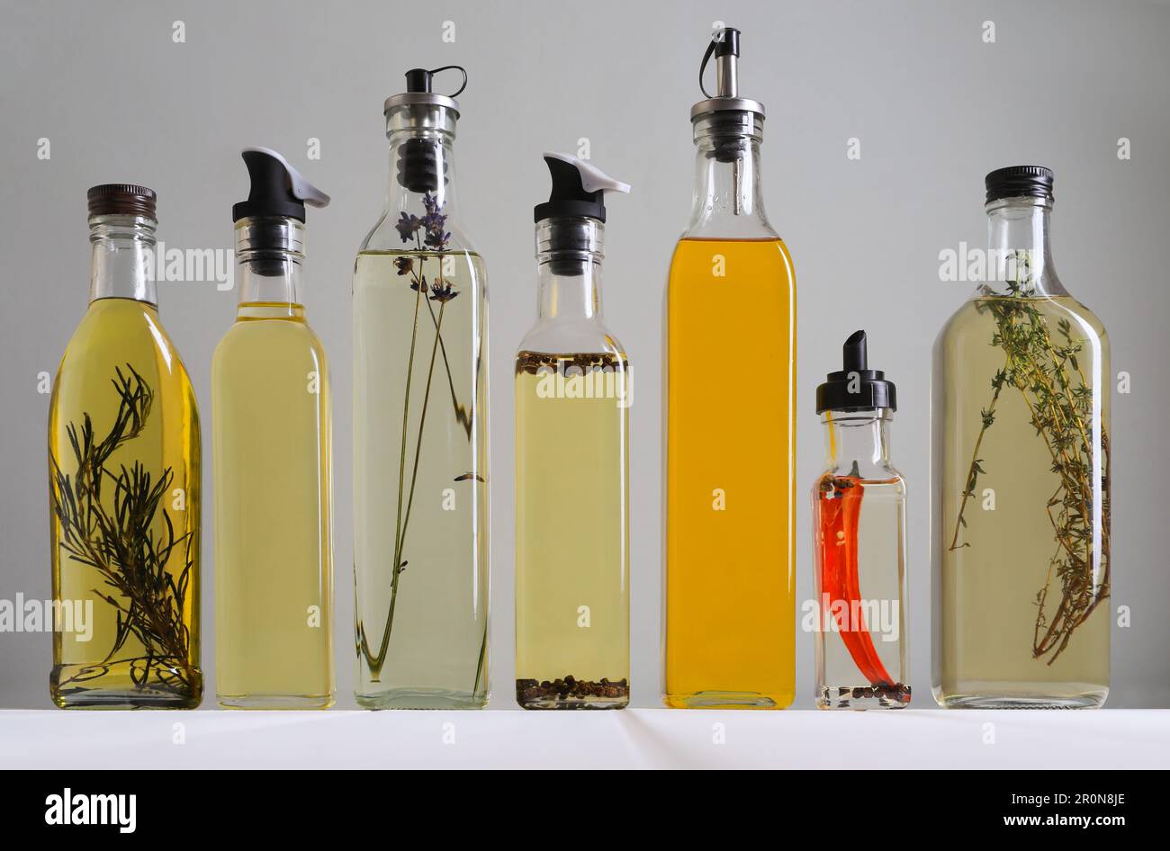 Bottles of different cooking oils on white wooden table against grey ...