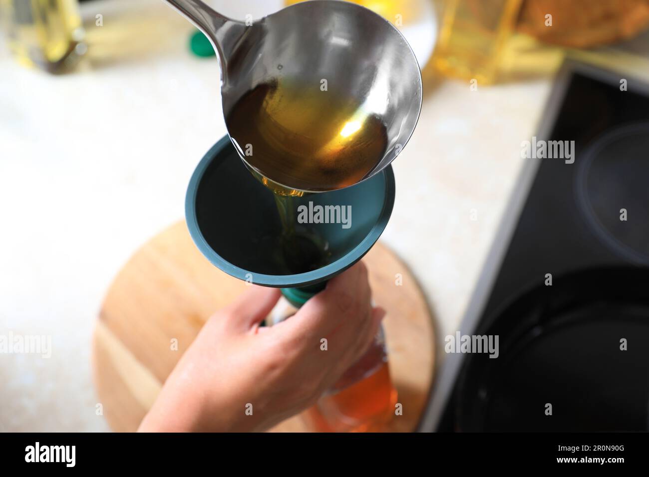 Woman pouring used cooking oil into bottle through funnel in kitchen ...