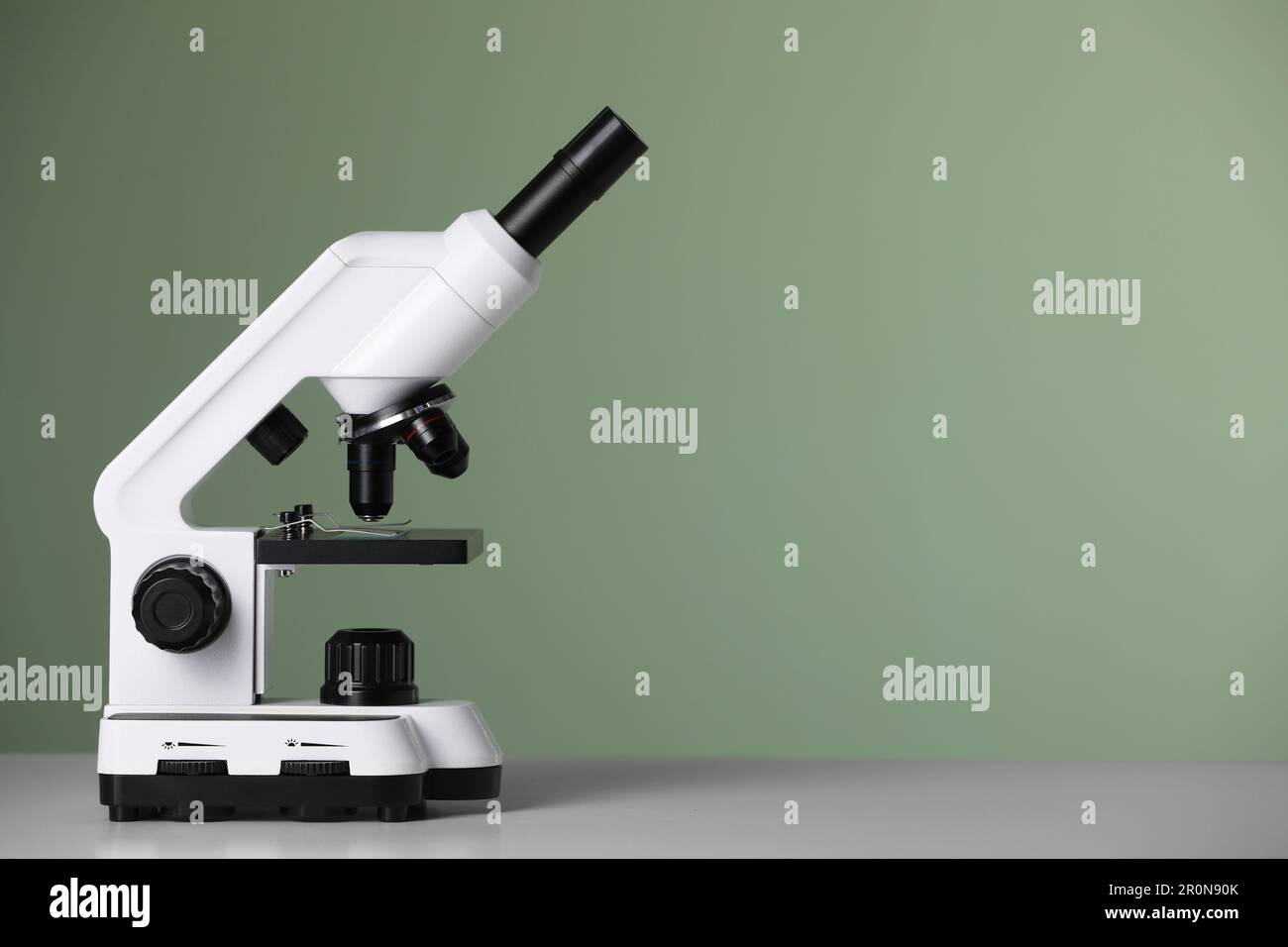 Modern microscope on table against green background. Space for text ...