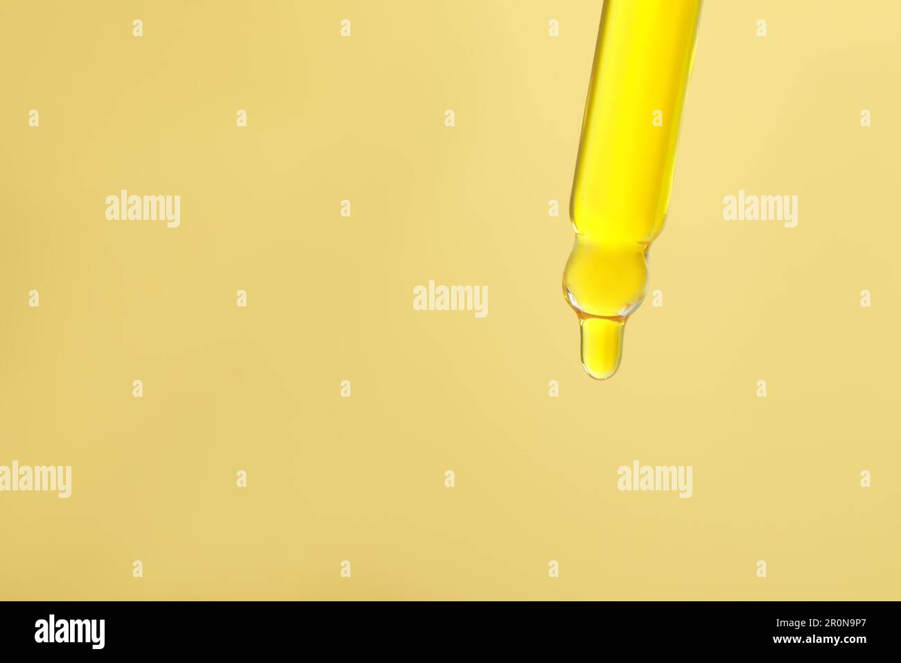 Dripping serum from pipette on yellow background, closeup. Space for ...