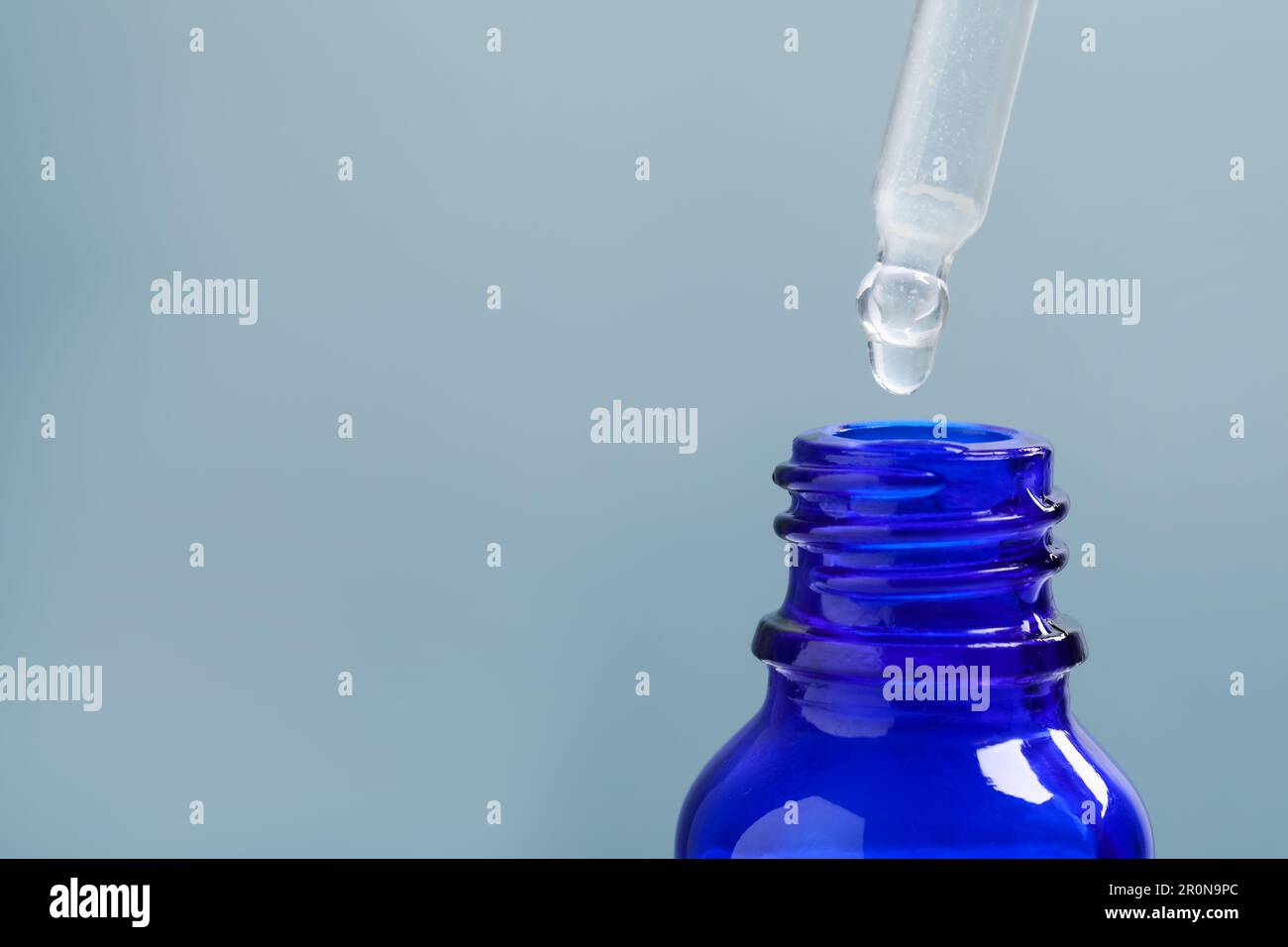 Dripping serum from pipette into bottle on grey background, closeup ...