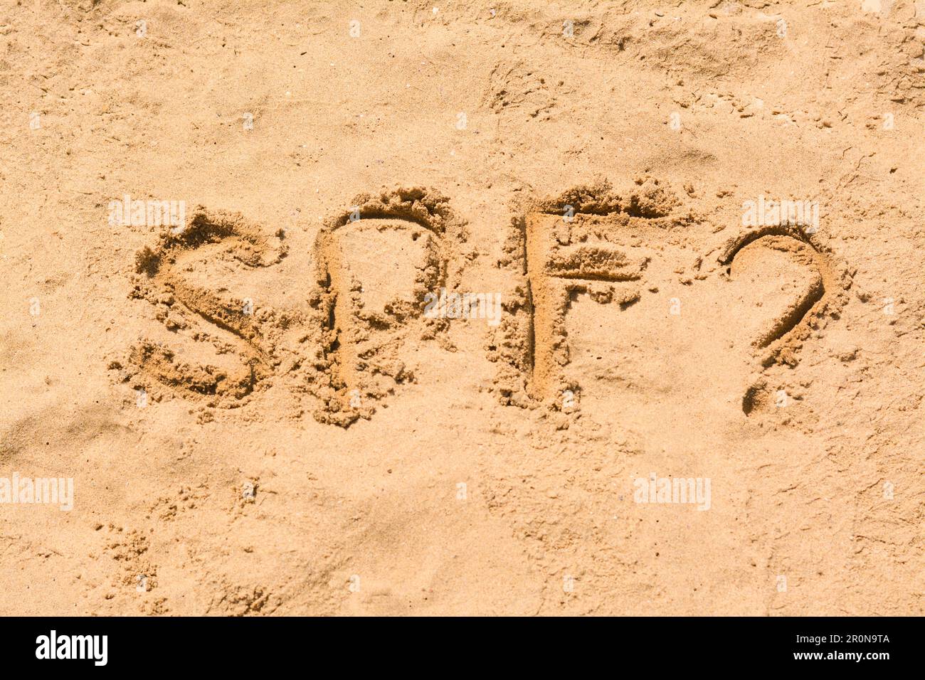 Abbreviation SPF and question mark written on sand at beach, above view ...