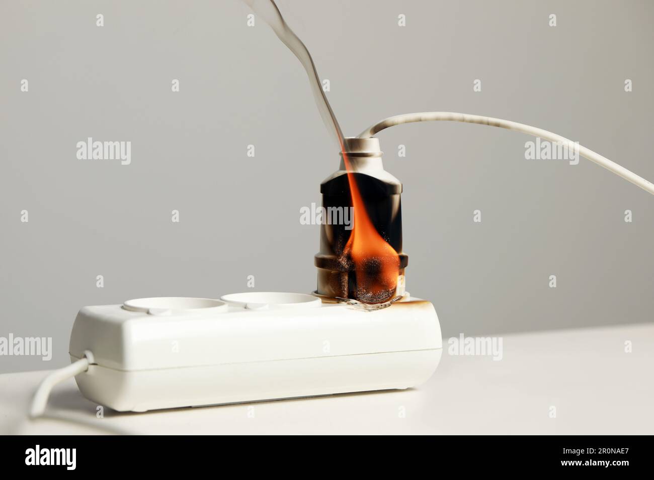 Inflamed plug in power strip on white table against grey wall ...