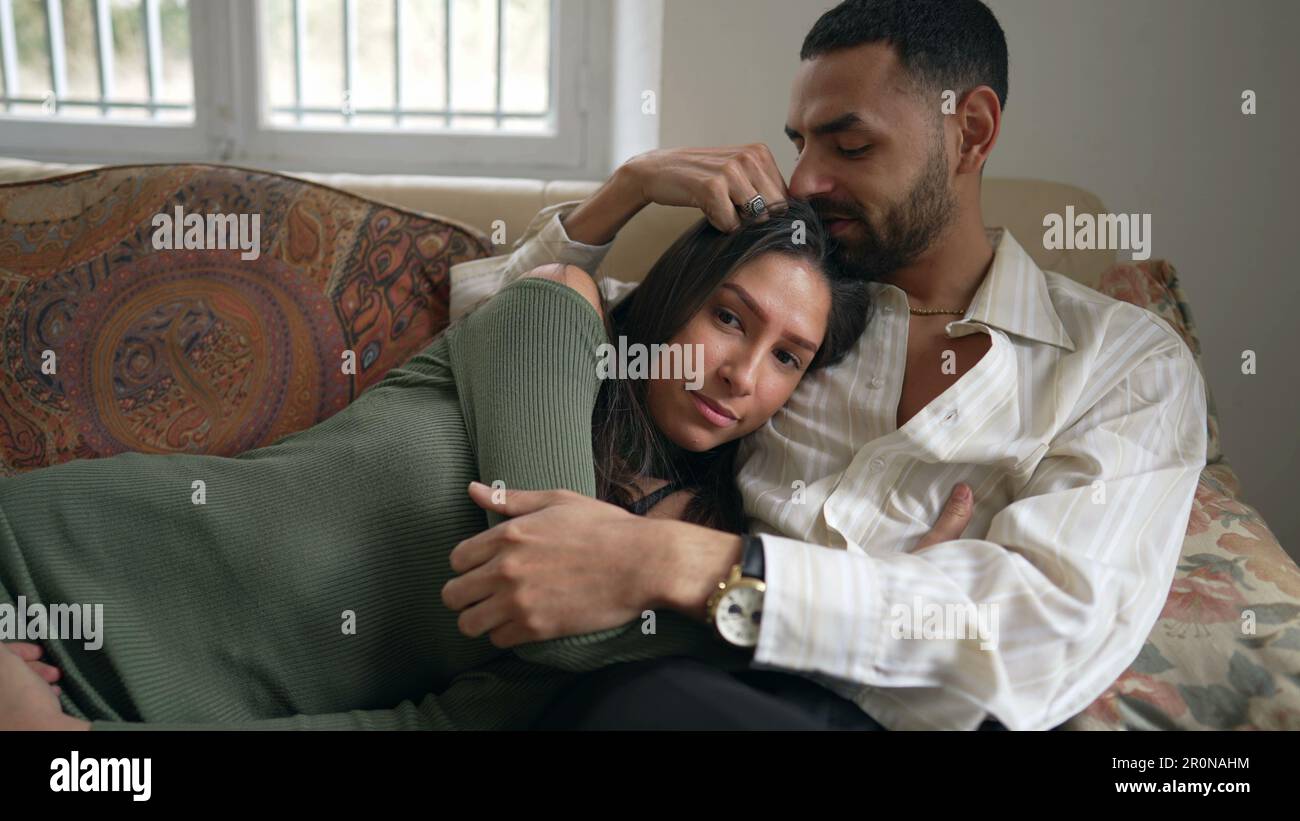 Caring assertive young boyfriend embracing girlfrined sitting on couch at home. Confident man ...