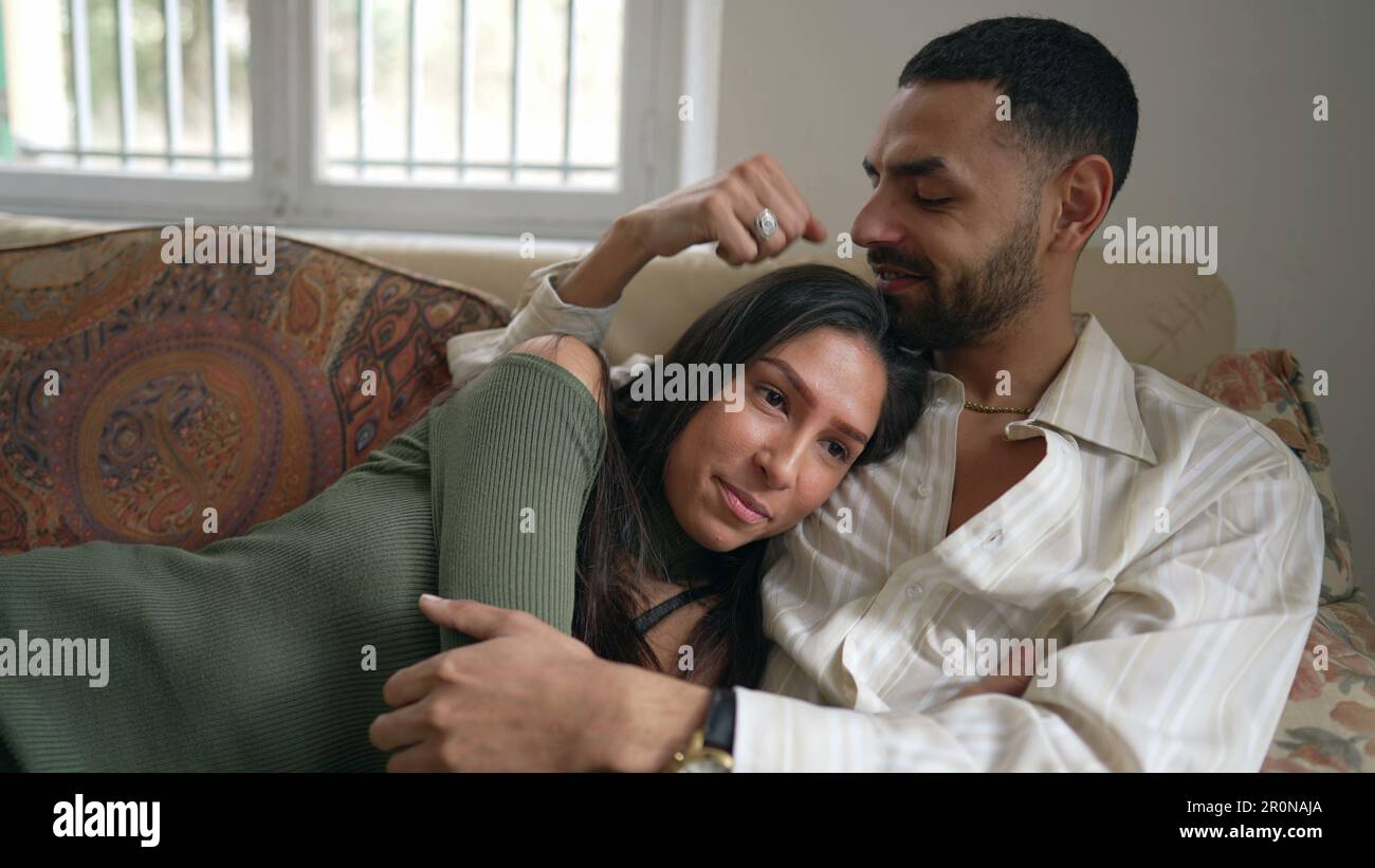 Caring assertive young boyfriend embracing girlfrined sitting on couch at home. Confident man ...