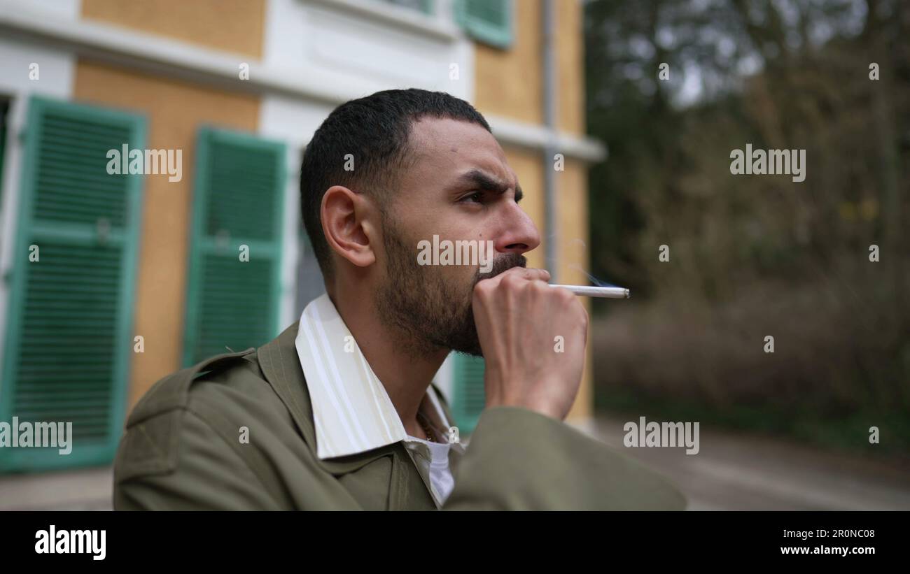 One pensive serious young Middle Eastern man smoking a cigarette ...