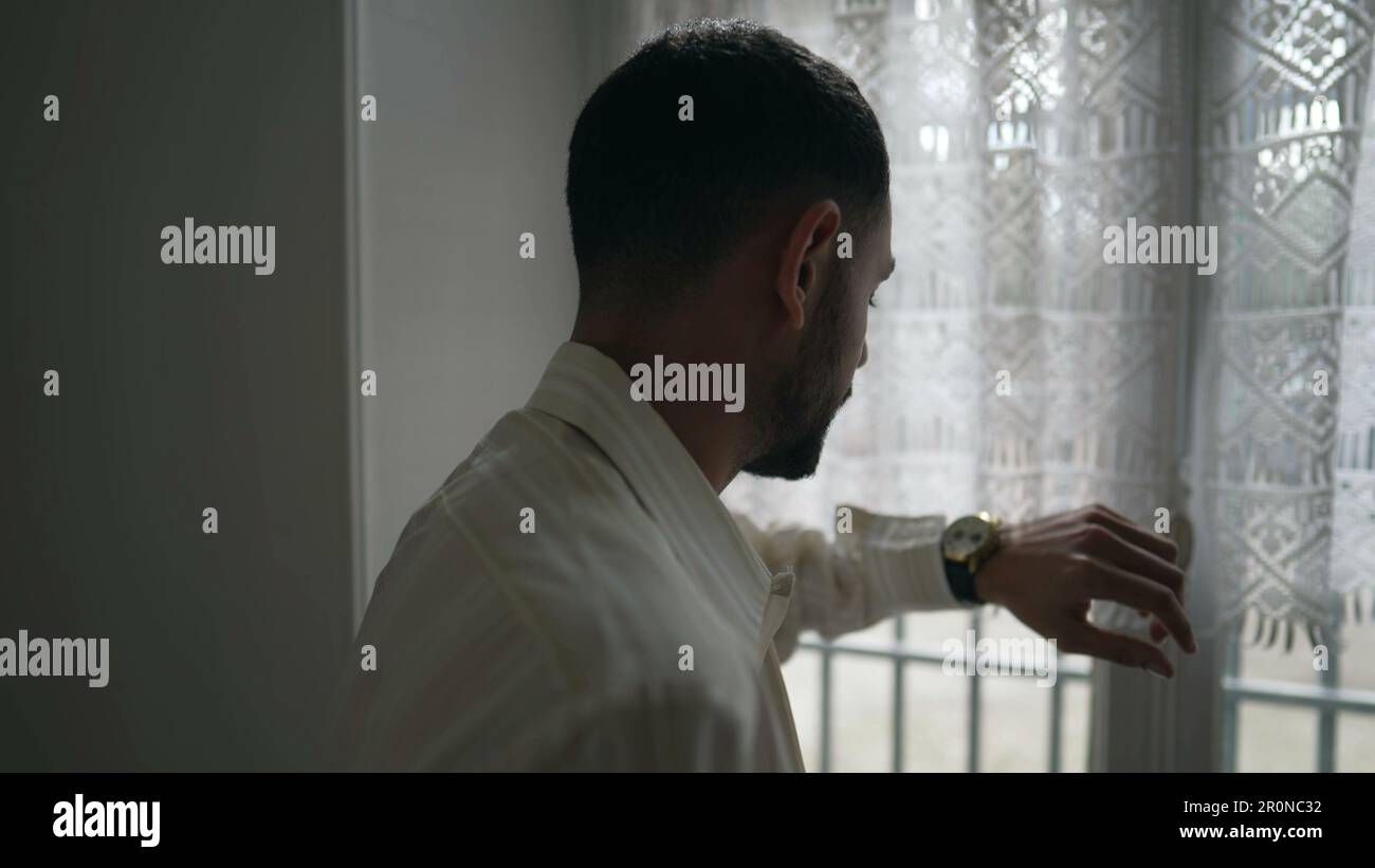 One pensive young Arab man standing by window waiting in standby while ...