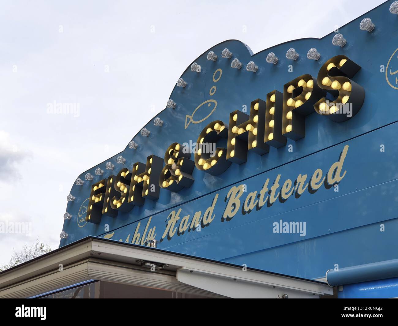 A vibrant blue neon sign "fish and chips" mounted to the side of a grungy, worn building Stock ...