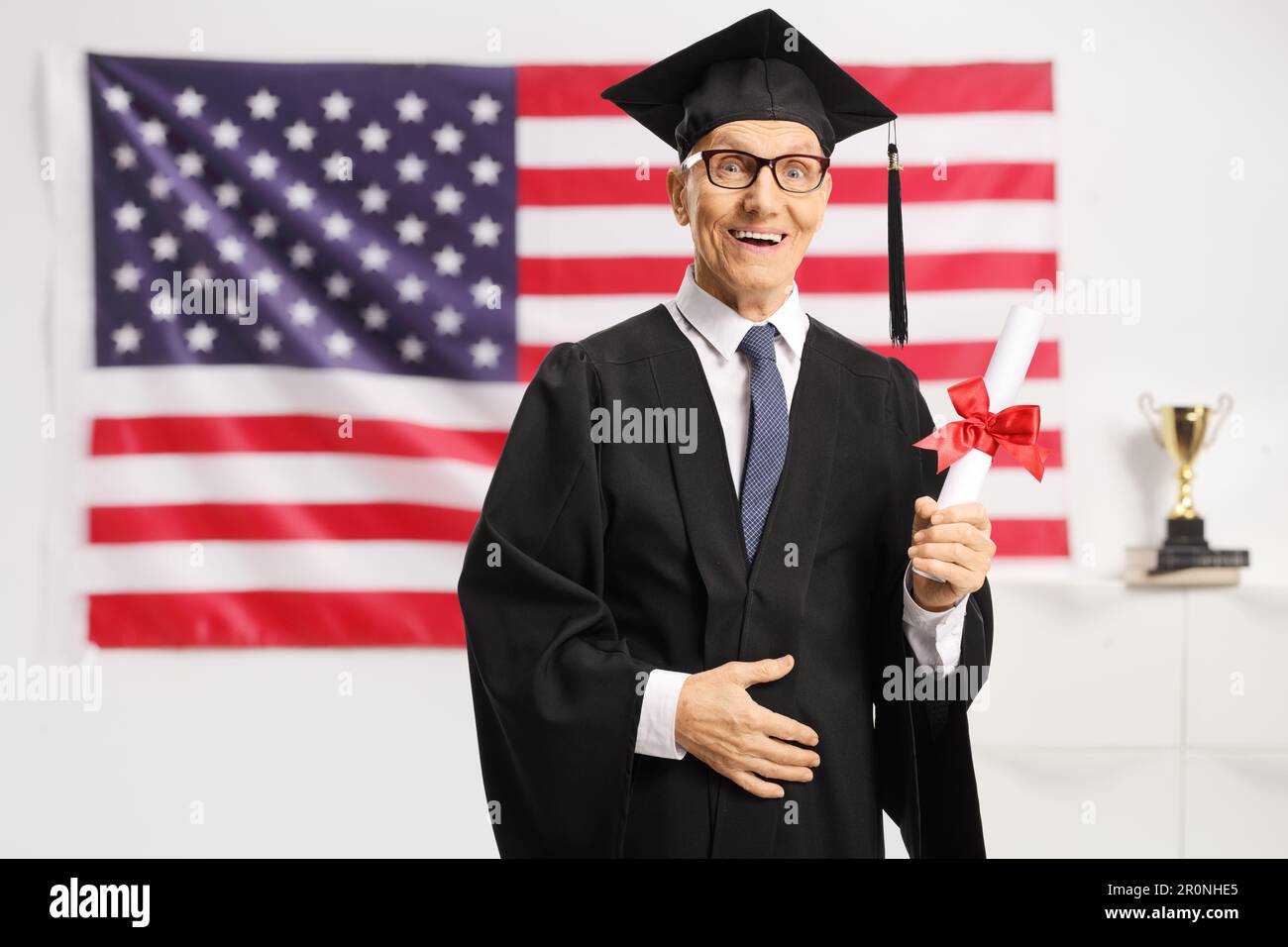 Senior man in a graduate gown holding a university degree in front of a ...