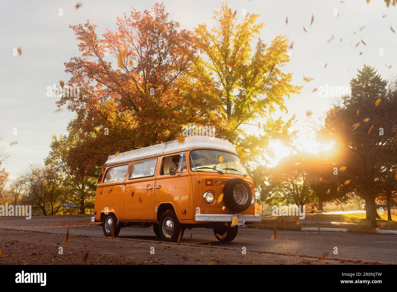 A vibrant orange camper van is parked in an autumnal setting ...