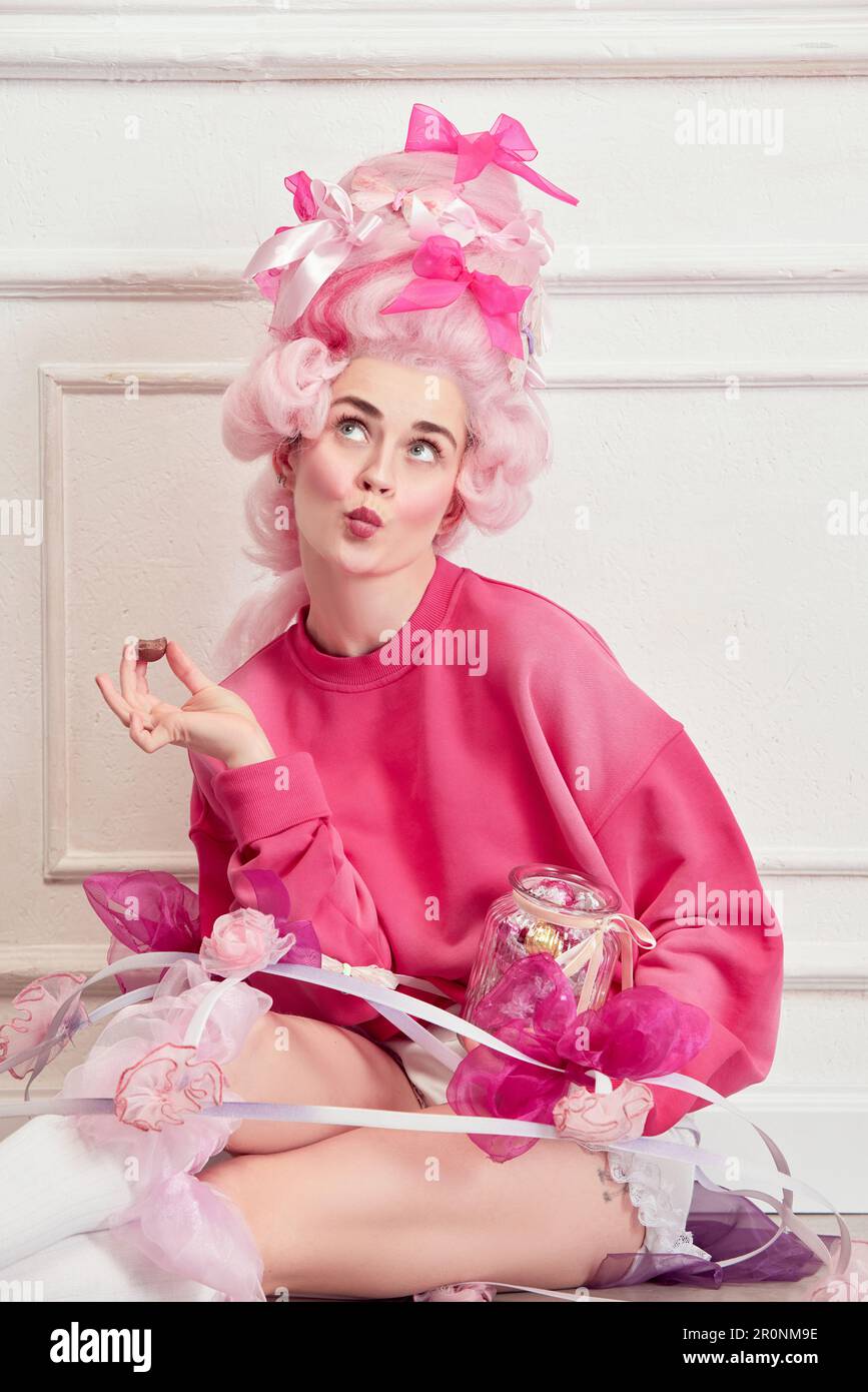 Portrait of beautiful woman, queen wearing pink wig and eating candies ...