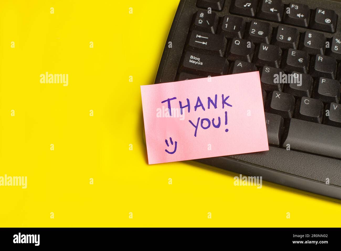 A black computer keyboard and a pink paper note with thank you phrase ...