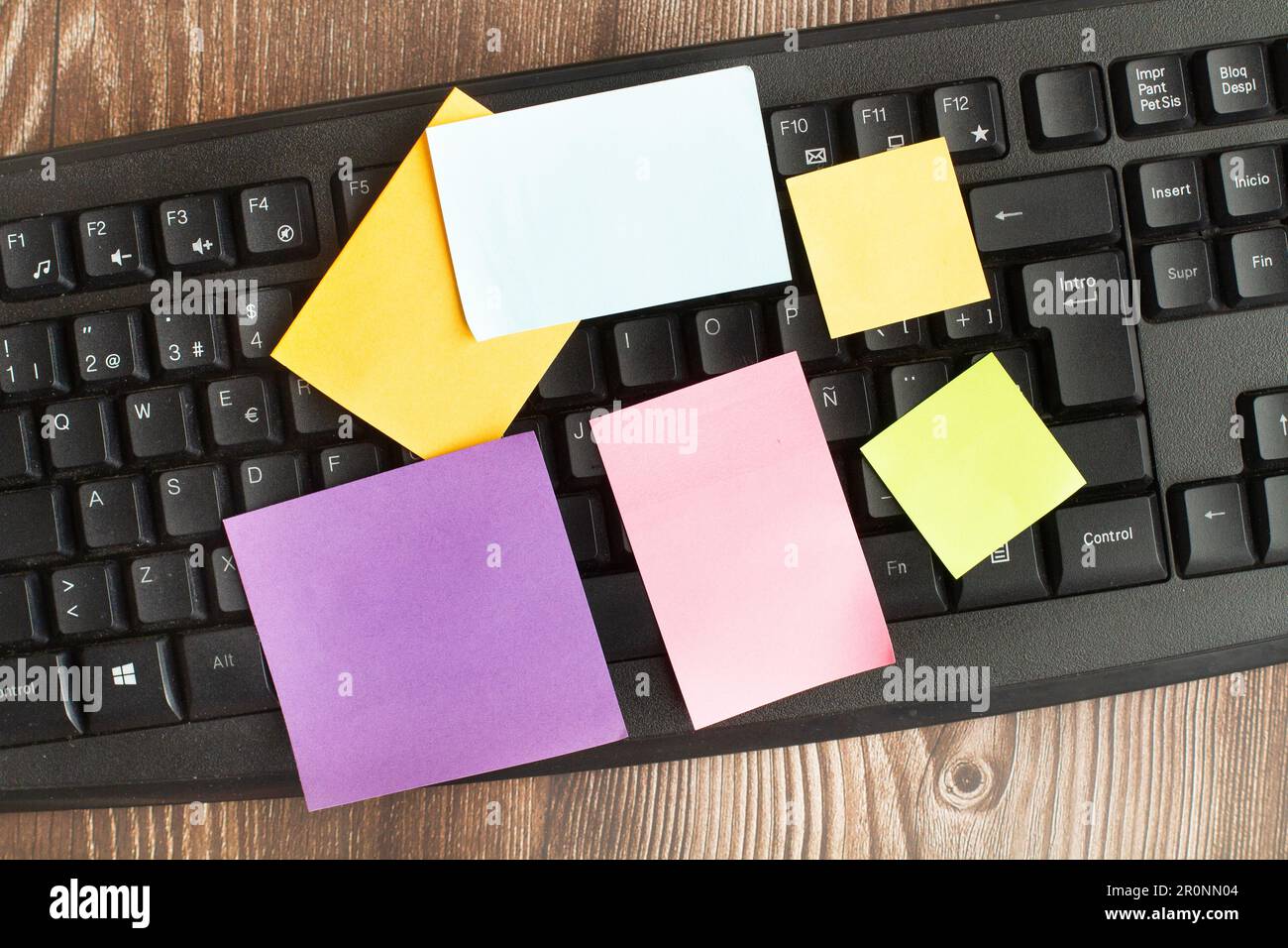 A black computer keyboard with colored paper notes on a wooden desk un ...
