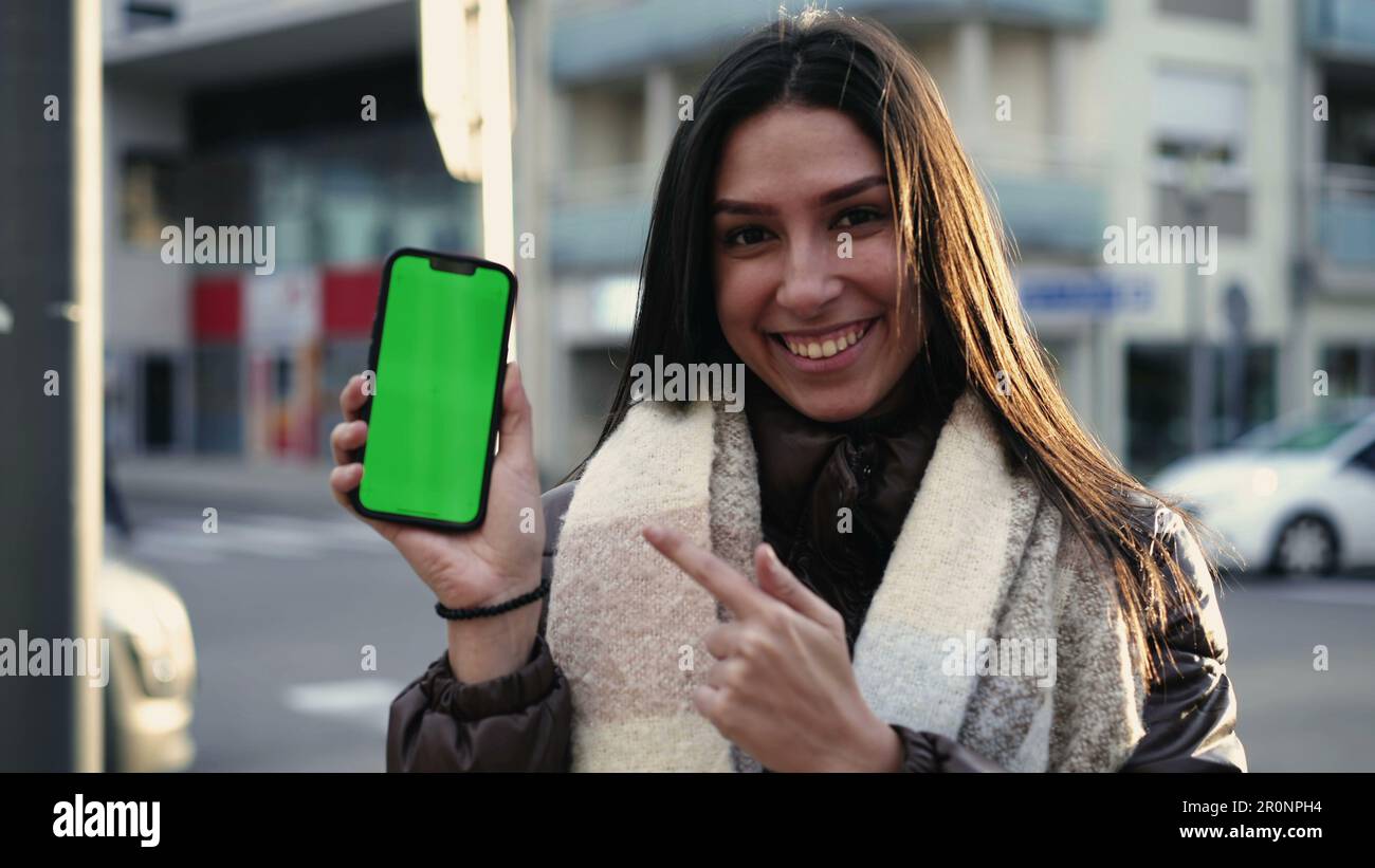 cheerful young woman presenting content on phone with chroma key ...