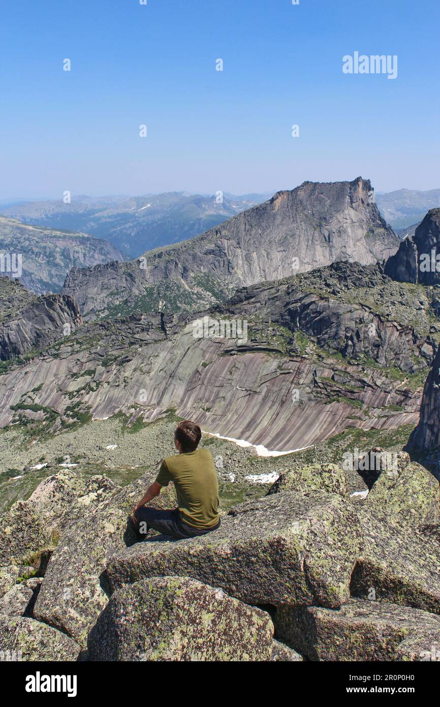 Man tourist sits on a rock high in the mountains. Panoramic view of a ...