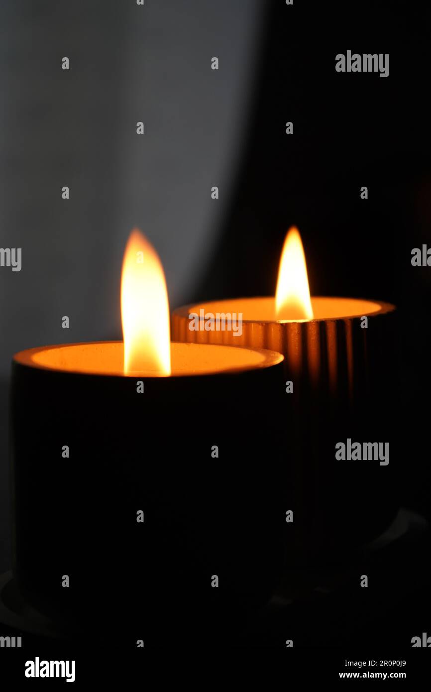 A set of lit white candles flickering in the dark on a black background ...
