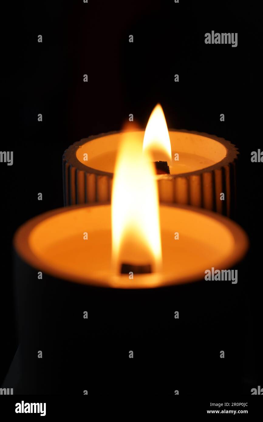 A set of lit white candles flickering in the dark on a black background ...