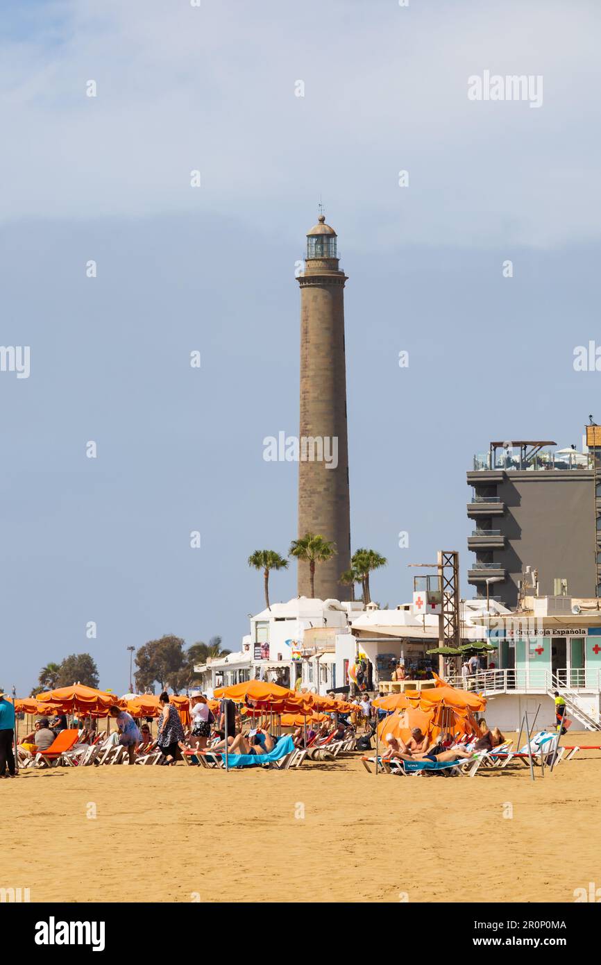 Tourists on the beach under orange umbrellas with the Maspalomas ...