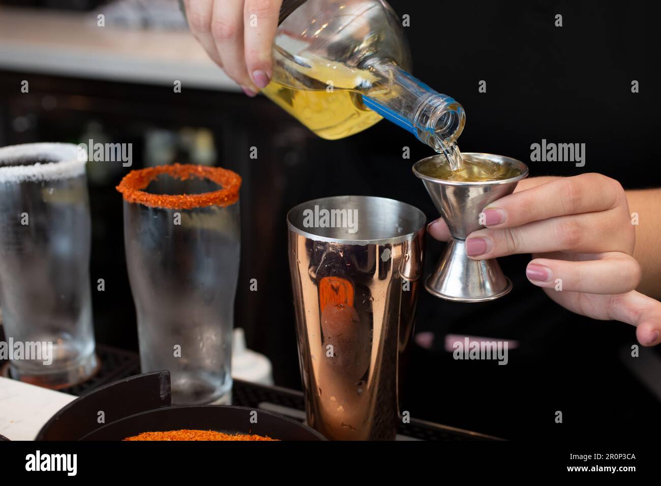 A view of a bartender using a jigger to measure a shot of liquor for ...