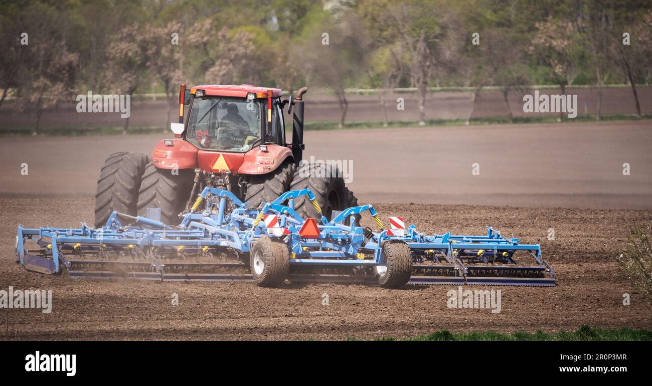modern tractor equipped with a cultivator plows a field in preparation ...