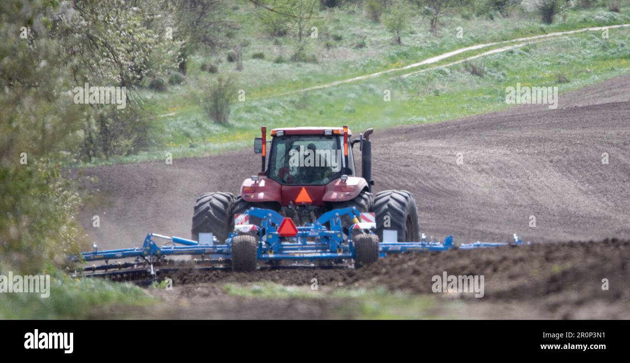 A tractor with a cultivator attachment tills the soil of a large field ...
