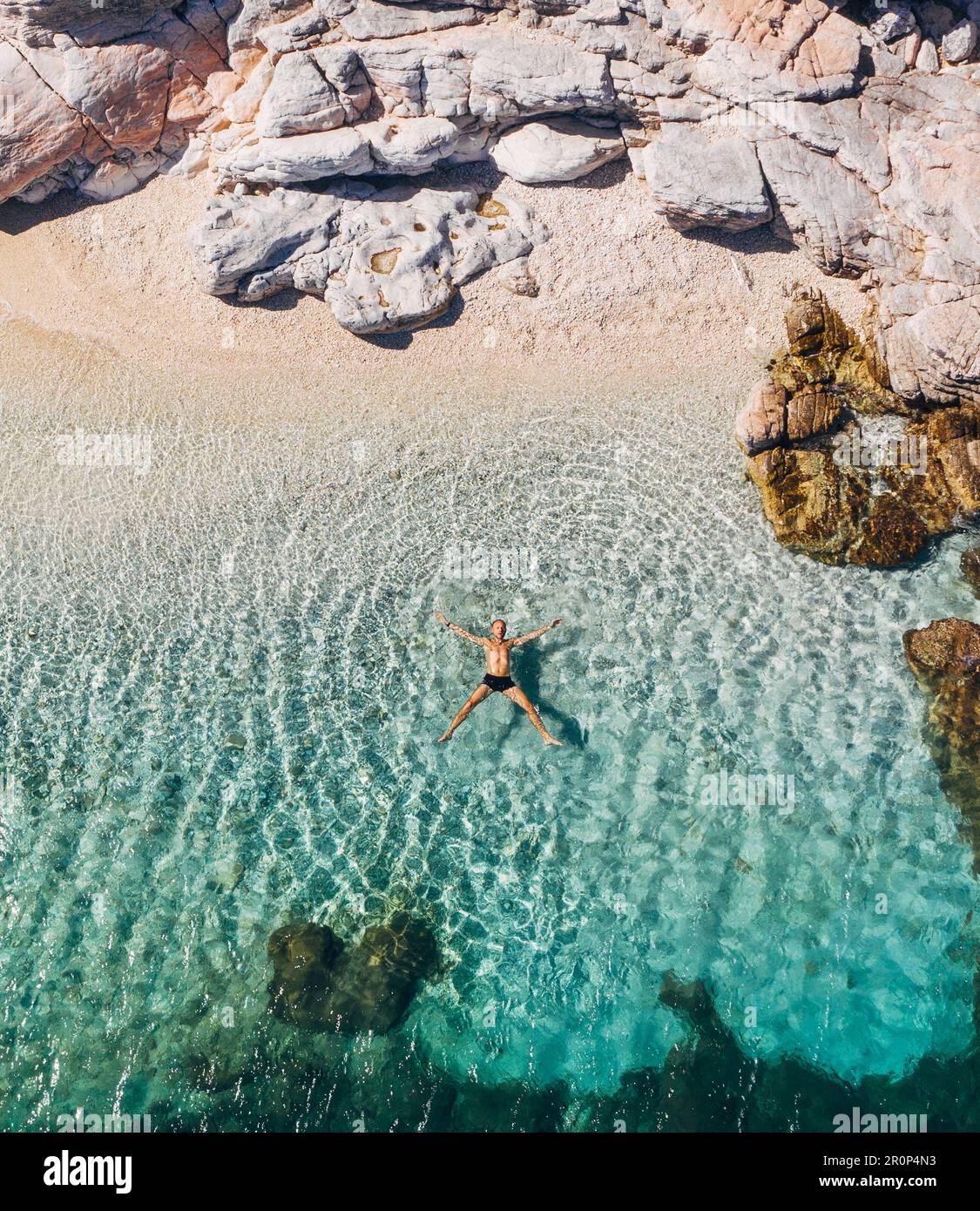 Aerial photo of man lying on the water in STAR pose on rocky pebbly ...