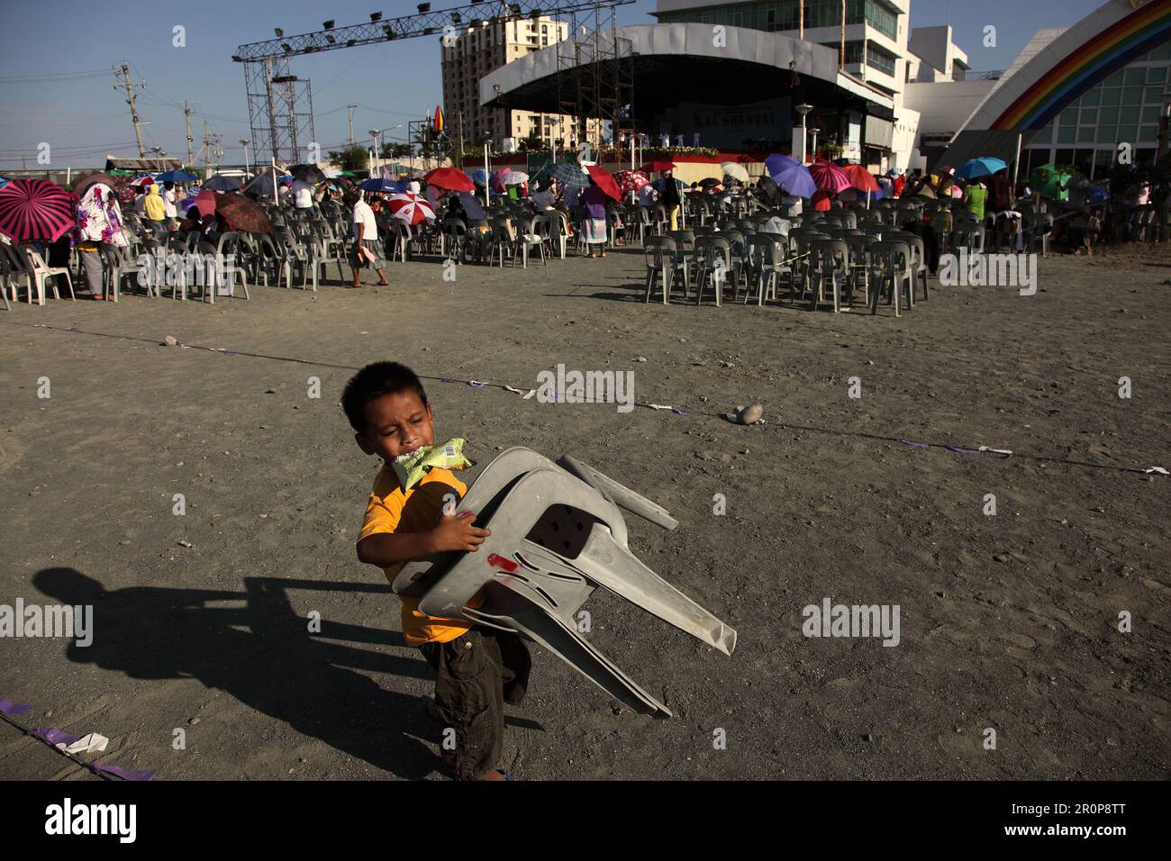A boy carrying chairs as people start to gather near the stage, hours ...