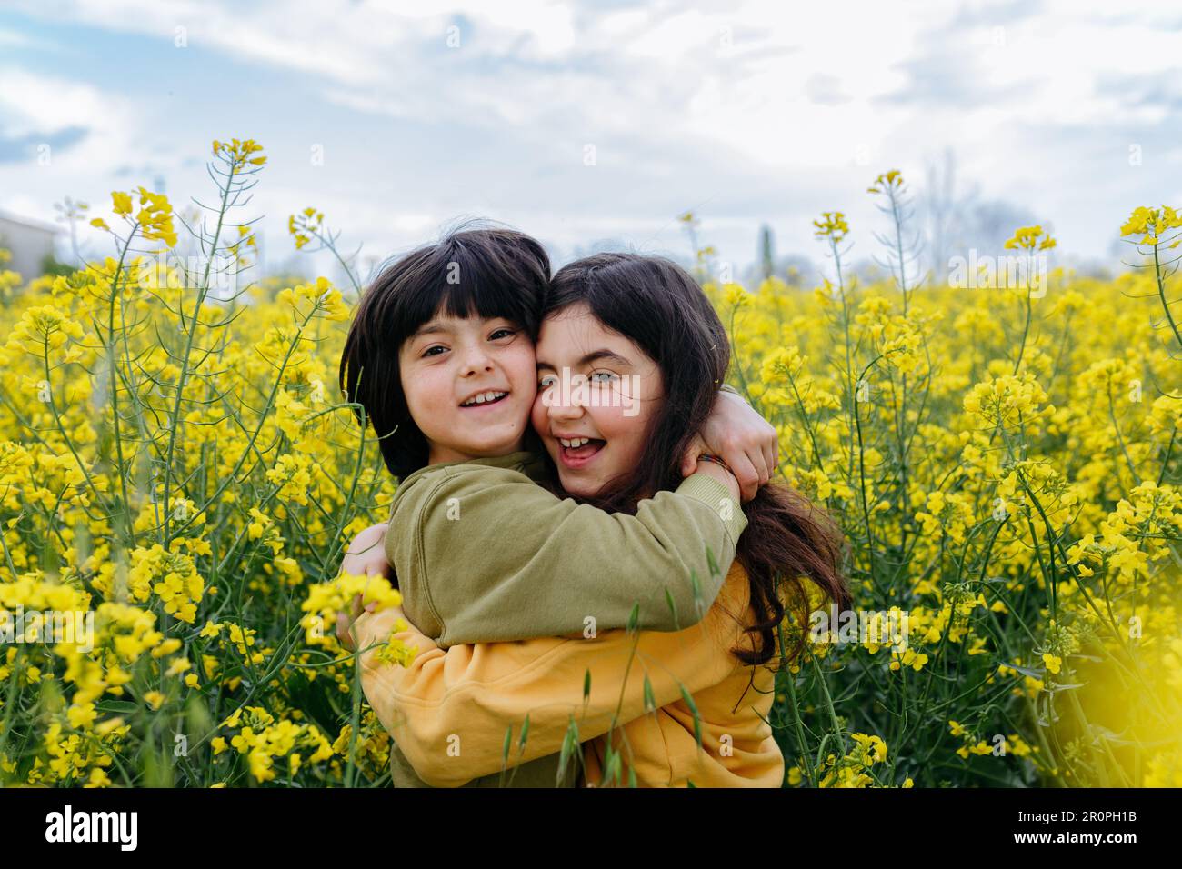 two happy sisters hugging each other in the field with yellow flowers ...