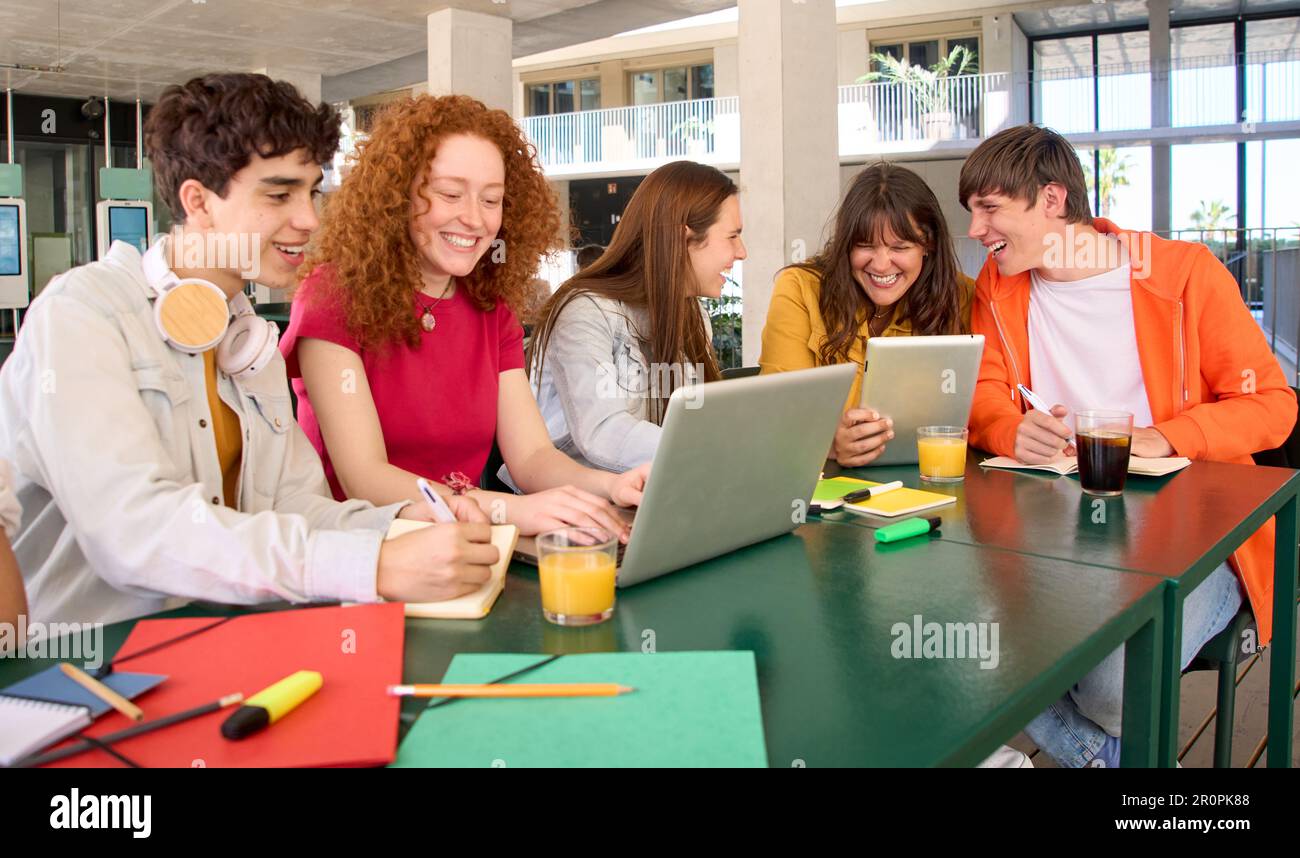 Smiling college classmates using laptops in campus cafeteria. Group ...