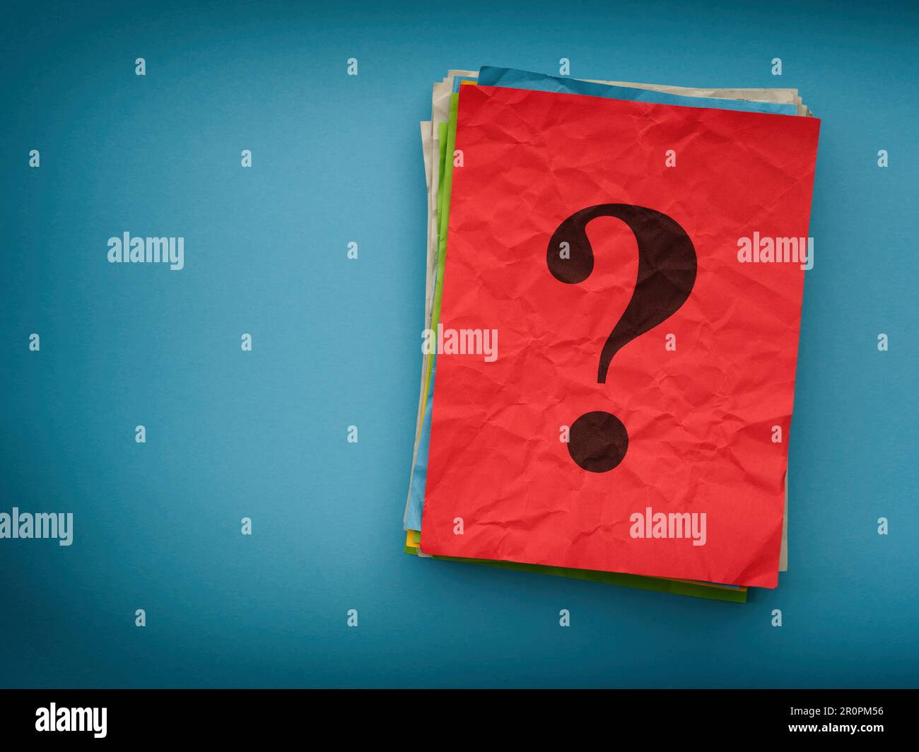 A stack of colorful paper notes with a question mark on them on a blue ...